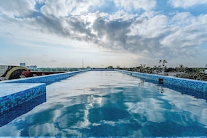 Uma piscina com azulejos de mosaico azul, rodeada por vegetação e um horizonte urbano ao fundo.