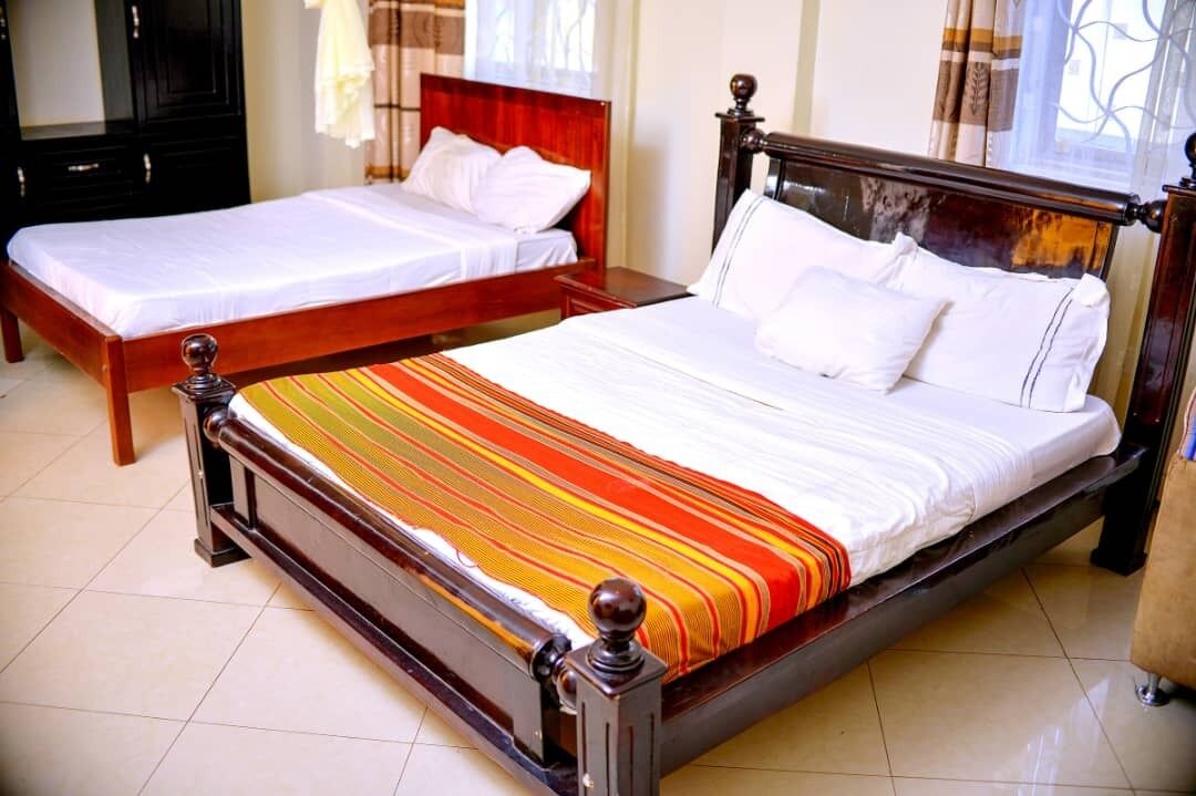 Quarto de hotel com duas camas de madeira, cada uma com roupa de cama branca e um cobertor listrado.