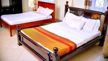 Quarto de hotel com duas camas de madeira, cada uma com roupa de cama branca e um cobertor listrado.