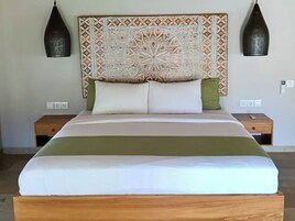 Uma cama com cabeceira estampada, duas mesas de cabeceira e um cobertor verde.