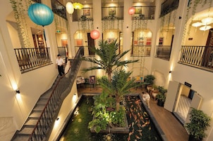 Um átrio de hotel com um elemento central de água, várias varandas e plantas em vasos.