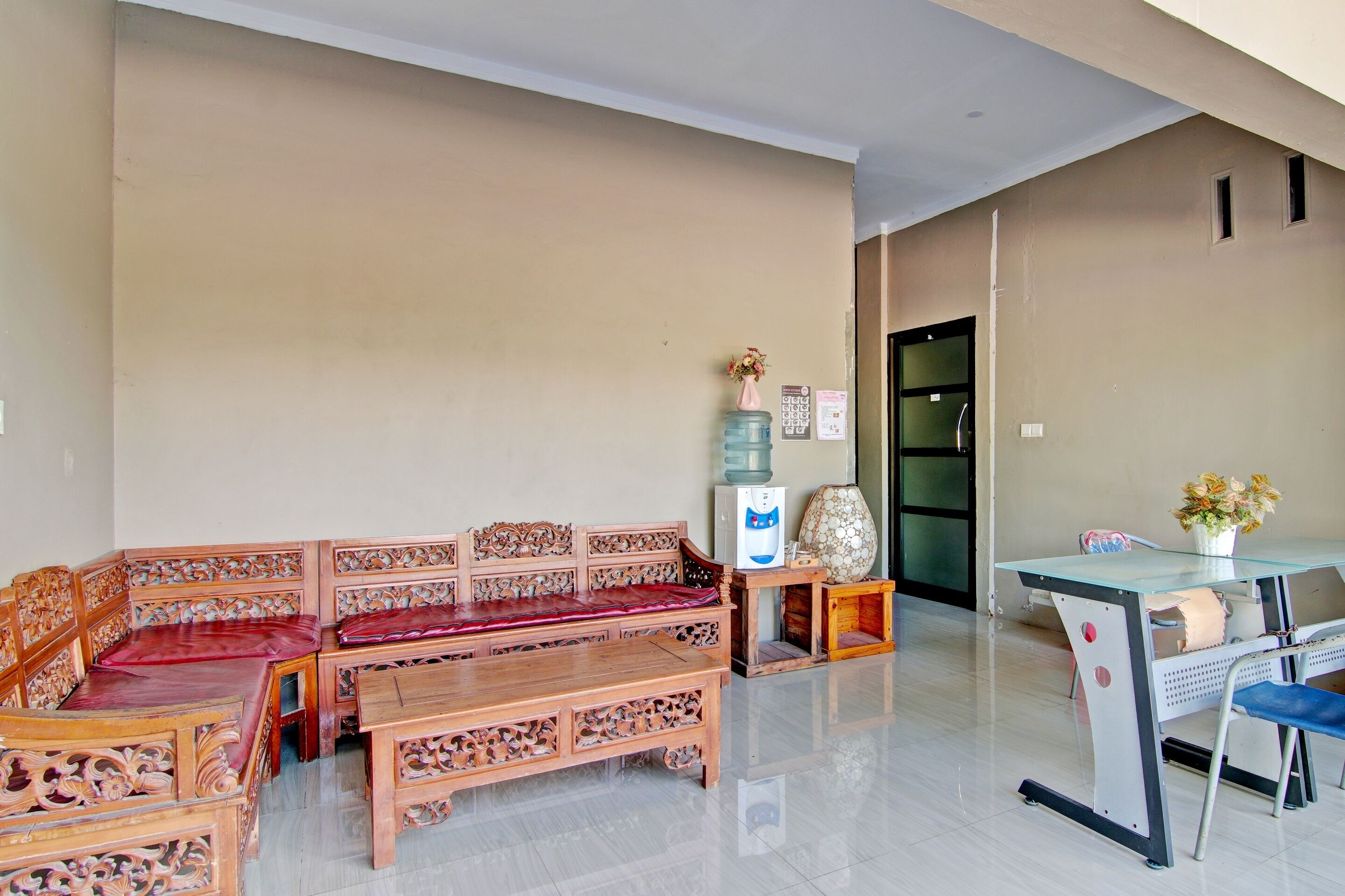 Quarto com sofá de madeira, mesa com tampo de vidro, dispensador de água e um pequeno armário.