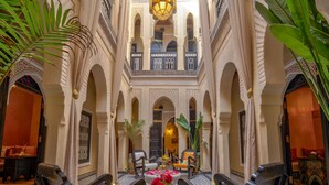 Um interior amplo com arcos altos, uma área de estar central com cadeiras e uma mesa, e uma fonte decorativa.