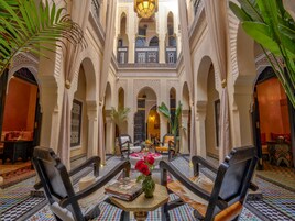 Um interior amplo com arcos altos, uma área de estar central com cadeiras e uma mesa, e uma fonte decorativa.