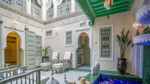 Um interior tradicional com arcos ornamentados, uma piscina com pétalas de flores flutuando e um espaço de estar com cadeiras e um candeeiro decorativo.