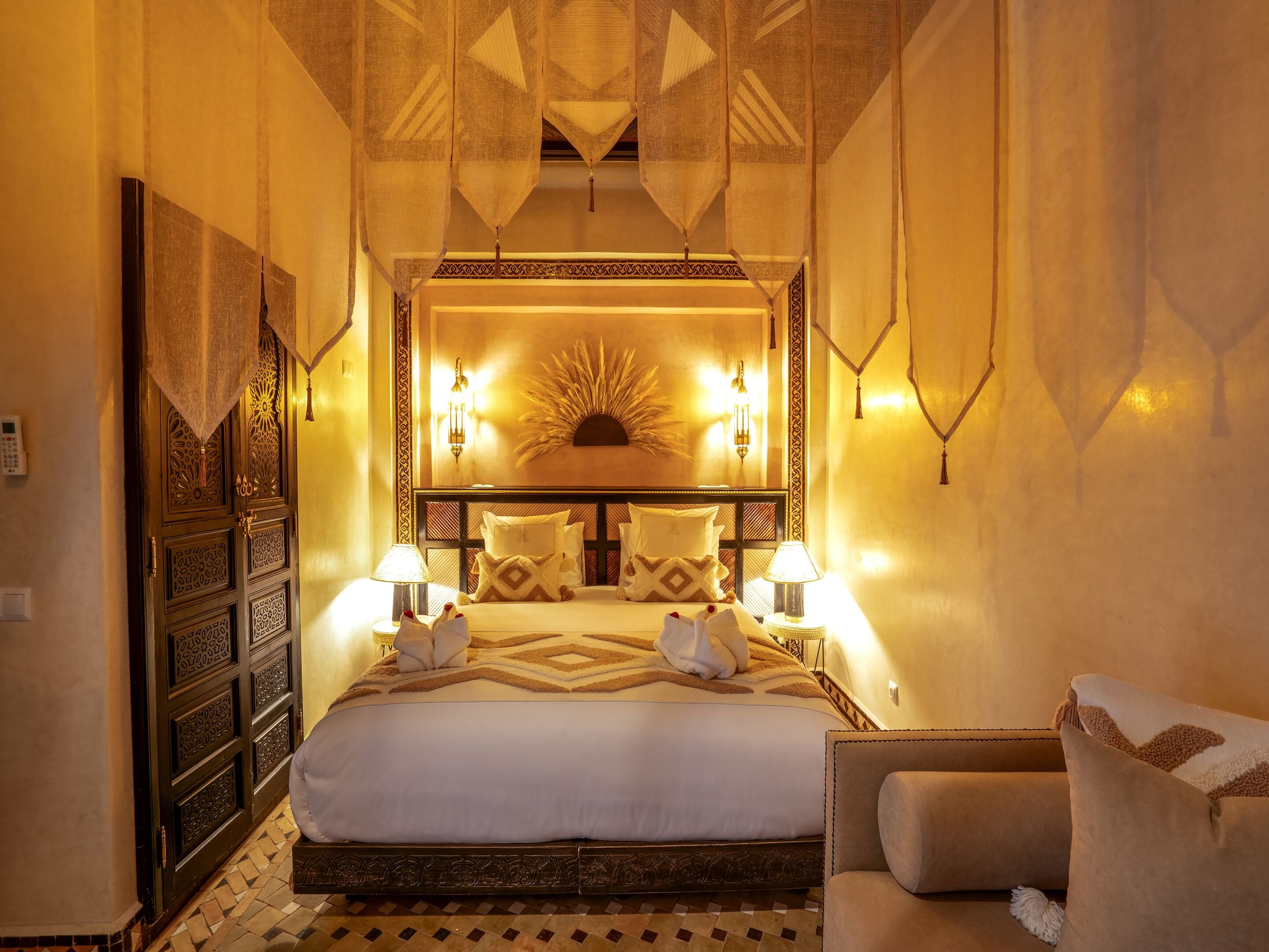 Quarto bem iluminado com uma cama grande, duas luminárias de cabeceira e um objeto decorativo sobre a cama.