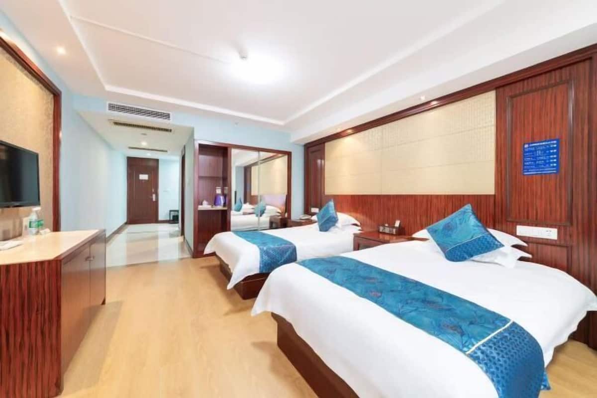 Quarto de hotel com duas camas, uma escrivaninha de madeira, televisão e espelho.