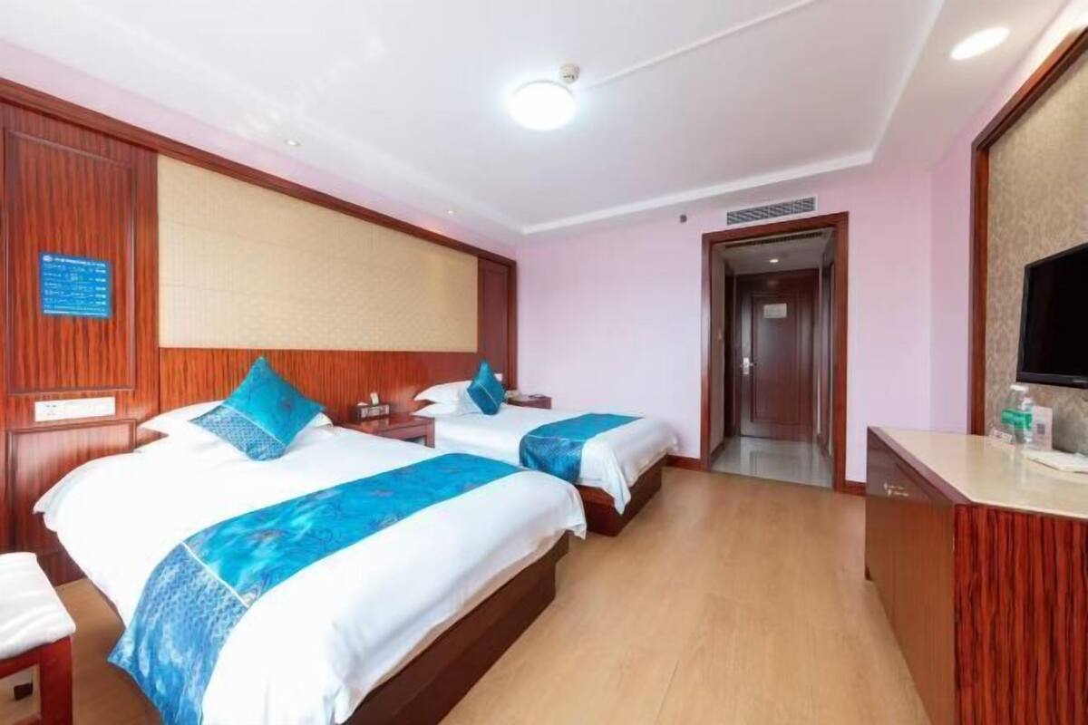 Quarto de hotel com duas camas, cabeceira de madeira, televisão e uma pequena mesa.