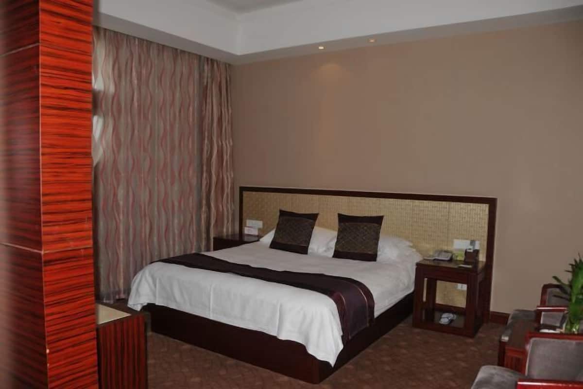 Quarto de hotel com uma cama grande, uma mesa de cabeceira, uma cadeira e uma pequena mesa com uma planta.