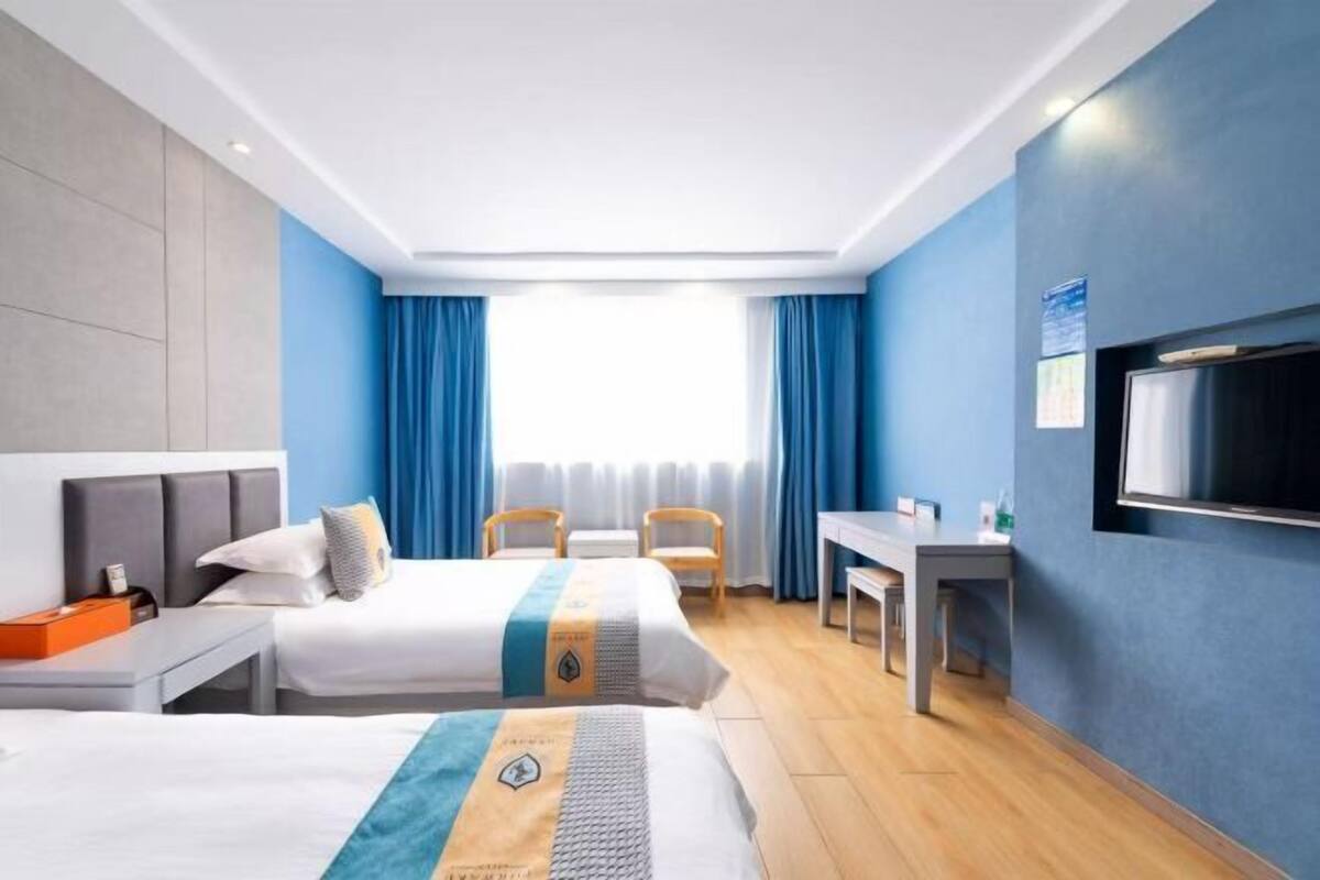 Quarto de hotel com duas camas, uma escrivaninha, uma televisão e uma janela com cortinas.
