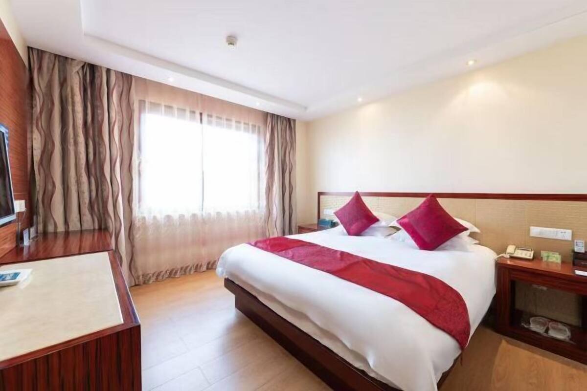 Quarto de hotel com cama, escrivaninha, televisão e janela com cortinas.