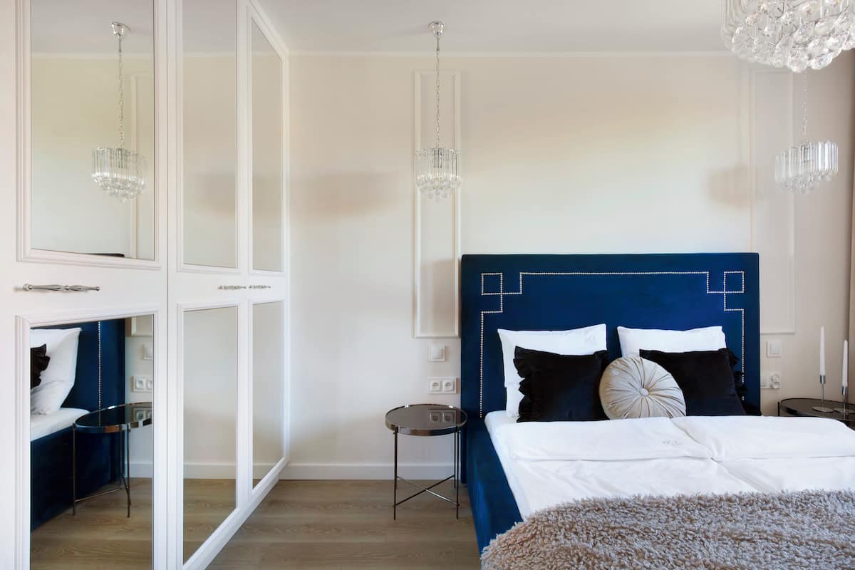 Quarto com uma cama grande, espelho, mesa pequena e lustre.