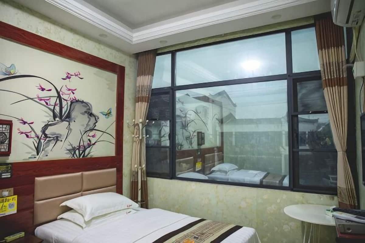 Quarto com cama, janela com cortinas, parede com mural floral e uma mesinha.
