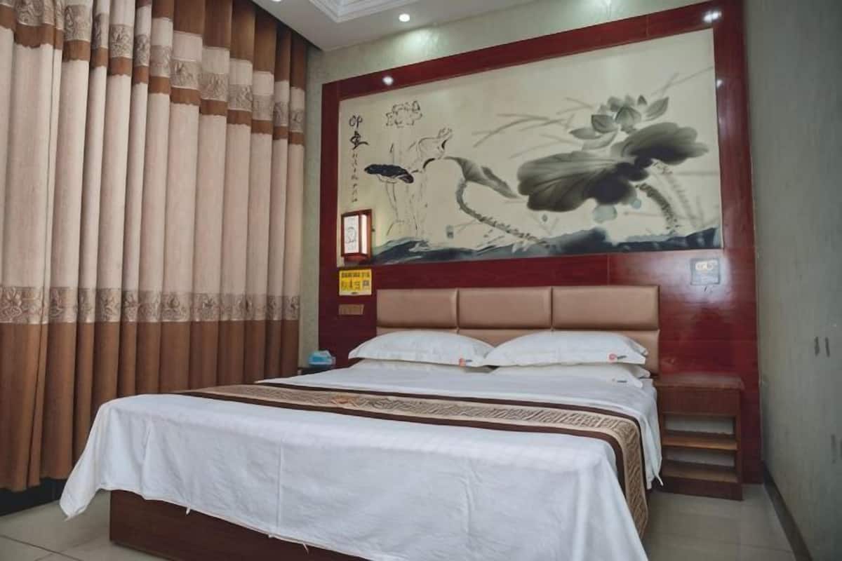 Quarto de hotel com uma cama grande, cabeceira com obra de arte e cortina com padrão tradicional.