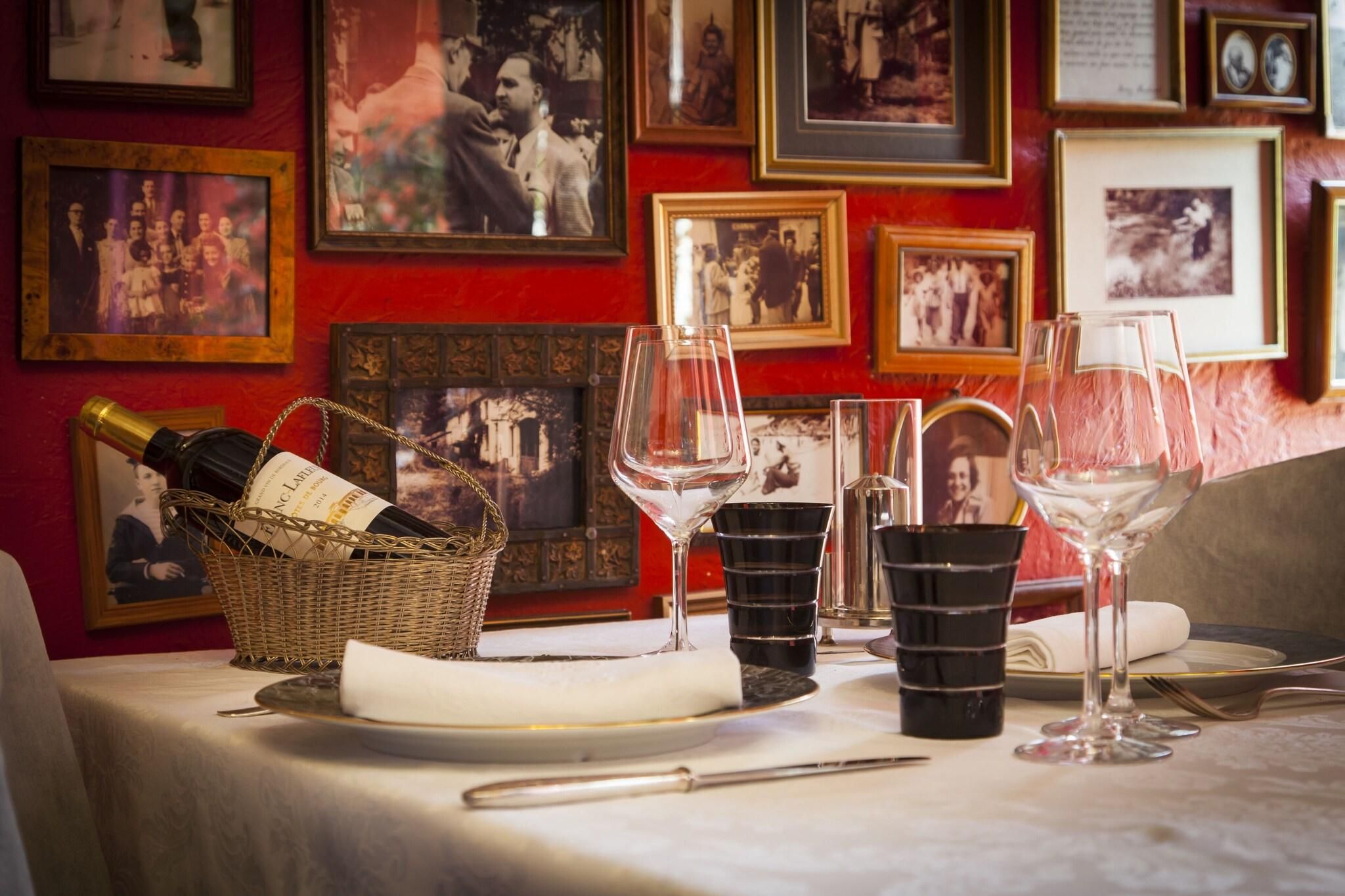 Uma mesa de jantar com copos de vinho, uma cesta de garrafas de vinho e xícaras pretas.