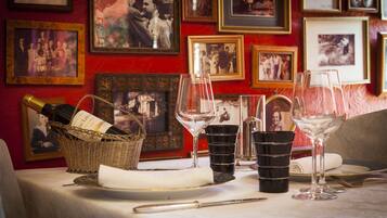 Uma mesa de jantar com copos de vinho, uma cesta de garrafas de vinho e xícaras pretas.