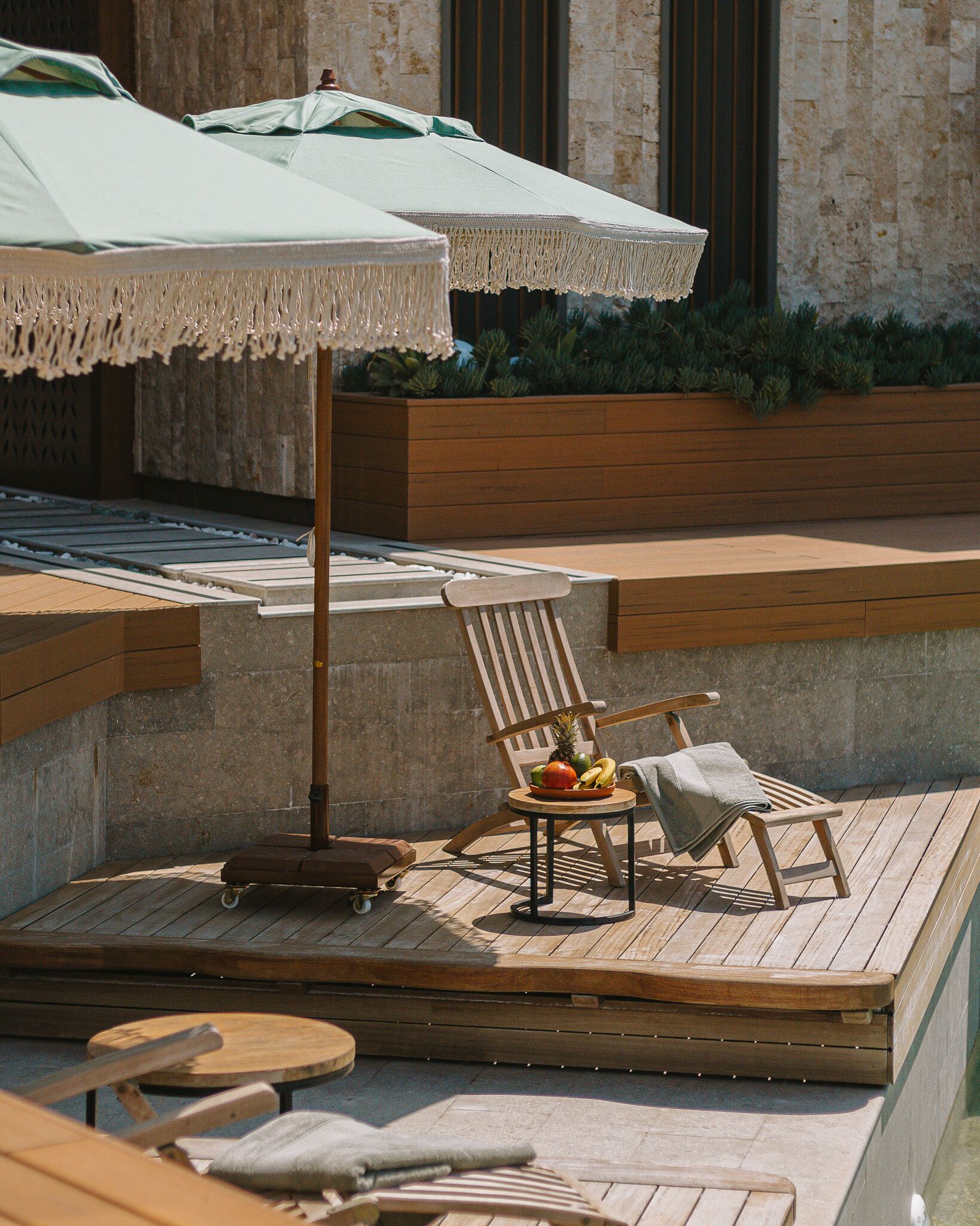 Um deck de madeira com móveis de exterior, incluindo uma cadeira e uma mesa, e um grande guarda-sol a dar sombra.