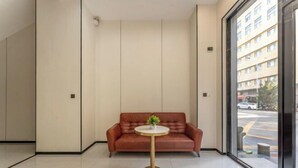 Um lobby moderno com um sofá de couro, uma mesa redonda com uma planta e uma grande janela com vista para a rua.