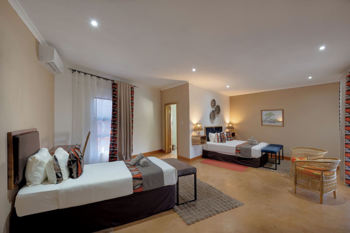 Quarto de hotel com duas camas, um espaço de estar, uma mesinha e uma cadeira.