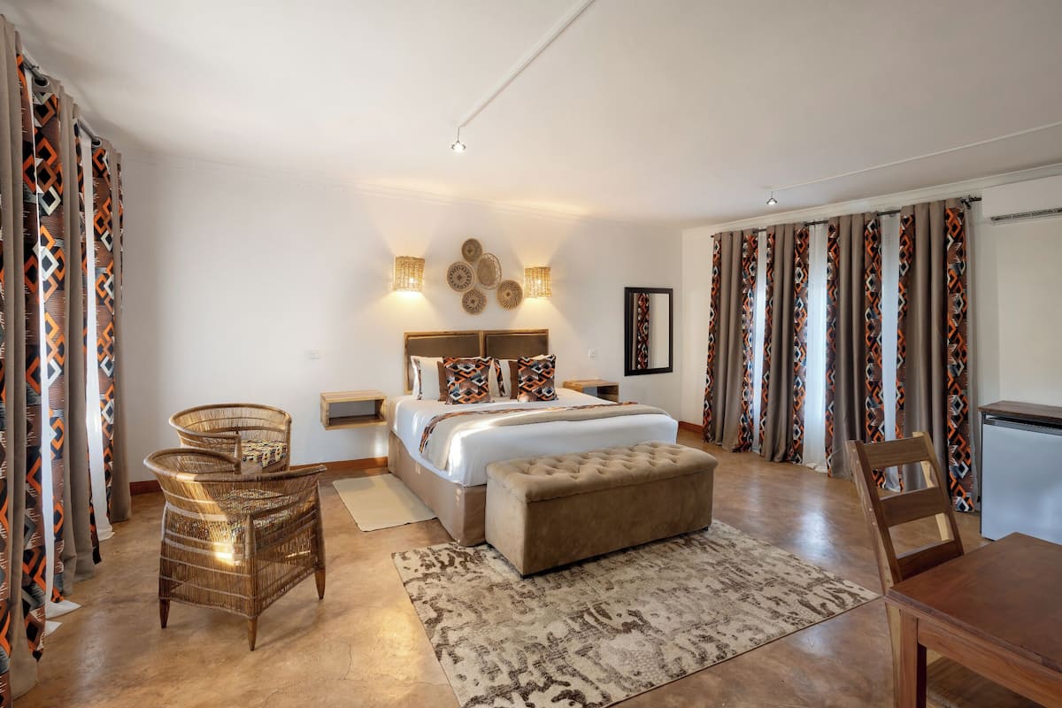 Quarto com uma cama grande, mesas de cabeceira, uma cadeira, uma pequena mesa e um espelho.