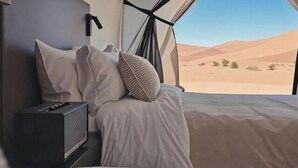Cama com travesseiros, mesa de cabeceira e vista das dunas do deserto.