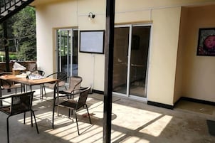 Quarto com mesa, cadeiras, televisão e porta de correr de vidro.