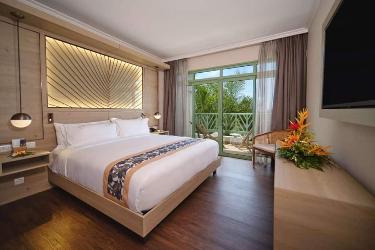 Quarto de hotel moderno com uma cama grande, uma mesa, uma cadeira e uma varanda com vista.