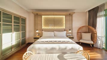 Quarto de hotel com uma cama grande, duas mesas de cabeceira, uma luminária na parede, uma cadeira de vime e uma janela grande com cortinas.