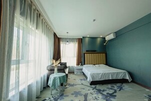 Quarto de hotel com uma cama, uma mesinha com um vaso, uma cadeira e uma janela com cortinas.