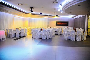 Uma sala de banquetes com mesas redondas, toalhas brancas e cadeiras.