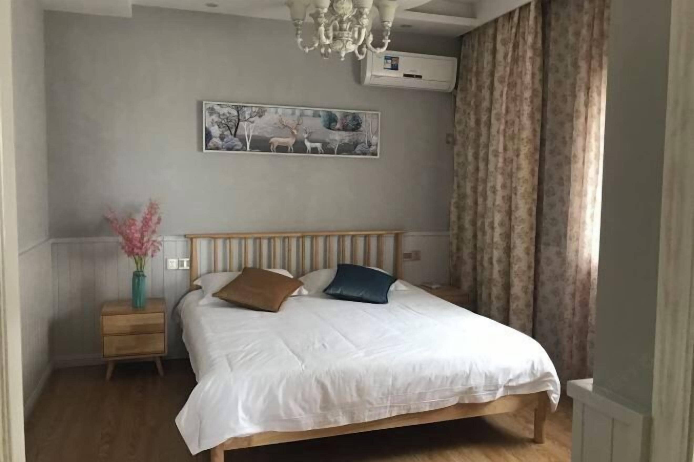Quarto com cama de madeira, mesa de cabeceira com um vaso, ar condicionado fixado na parede e uma pintura sobre a cama.