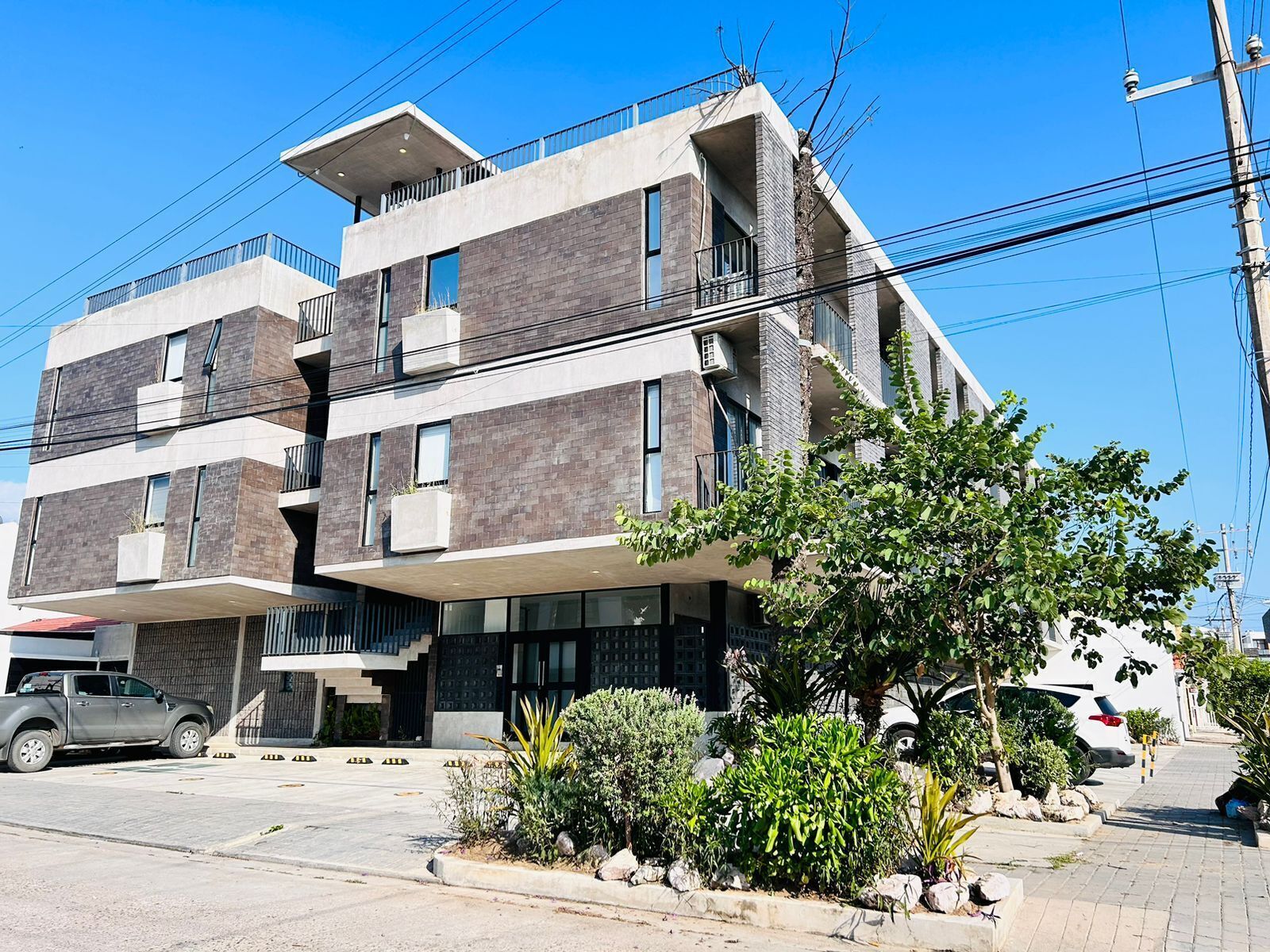 Edifício com vários andares, varandas, área de estacionamento e vegetação ao redor.