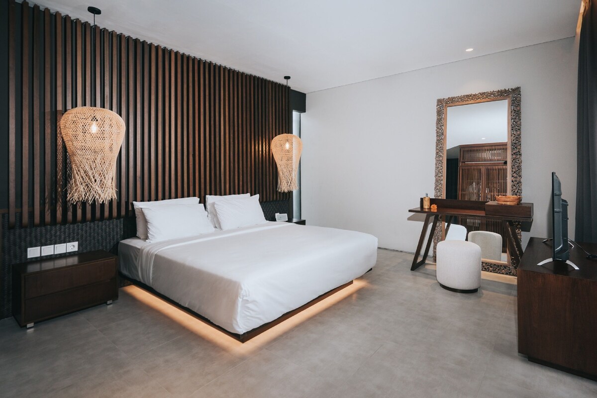 Quarto moderno com uma cama grande, cabeceira de madeira, mesa de cabeceira, espelho e televisão.