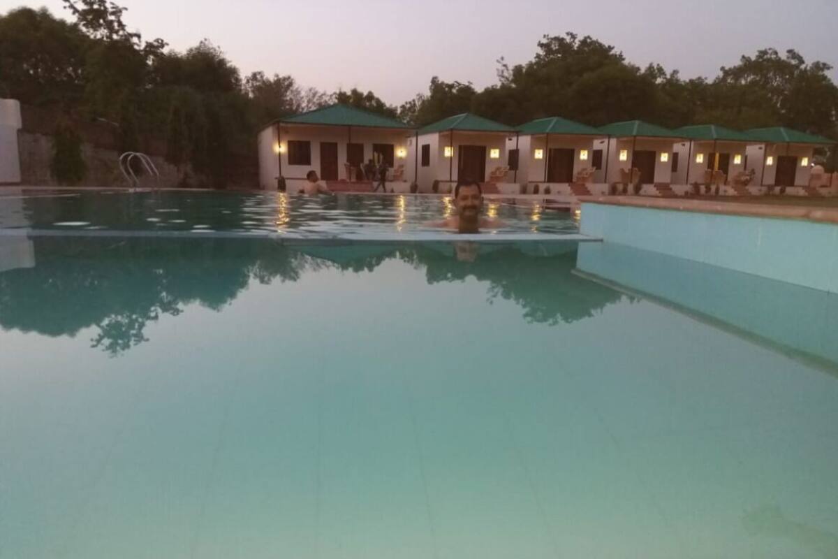 Piscina com espreguiçadeiras e um edifício com vários quartos ao fundo.