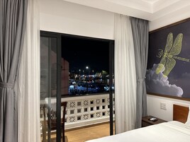 Quarto de hotel com varanda, cama, mesa de cabeceira e uma parede com uma obra de arte de libélula.