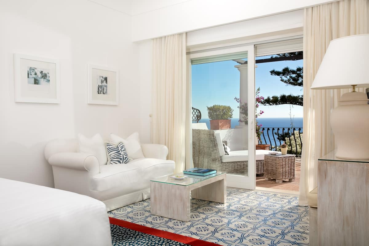 Uma sala de estar moderna com um sofá branco, uma mesa de centro de vidro e vista para o mar através de uma porta de correr.