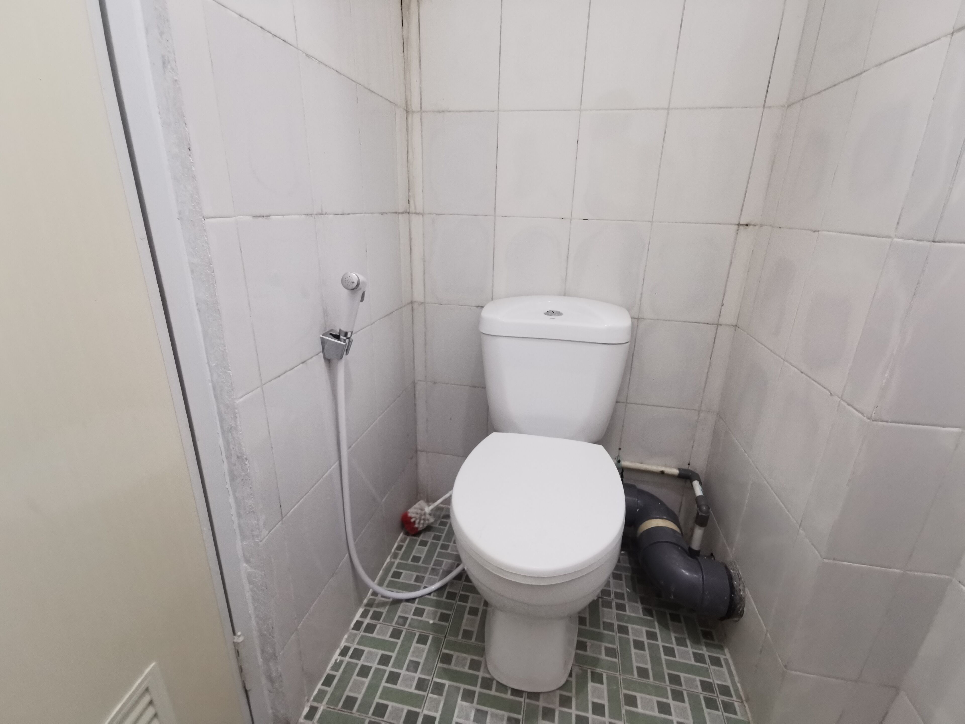 Um banheiro pequeno revestido com azulejos, com vaso sanitário, chuveiro e cano aparente.