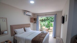 Quarto com cama, mesa de cabeceira, guarda-roupa e janela com vista para o verde lá fora.