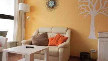 Sala de estar com sofá, mesa, abajur, relógio de parede e adesivo de árvore.
