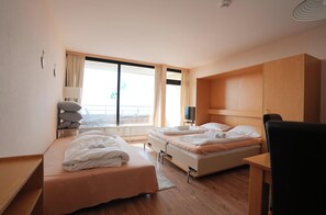 Quarto de hotel com duas camas, uma escrivaninha, uma cadeira, uma televisão e janela com vista para o exterior.