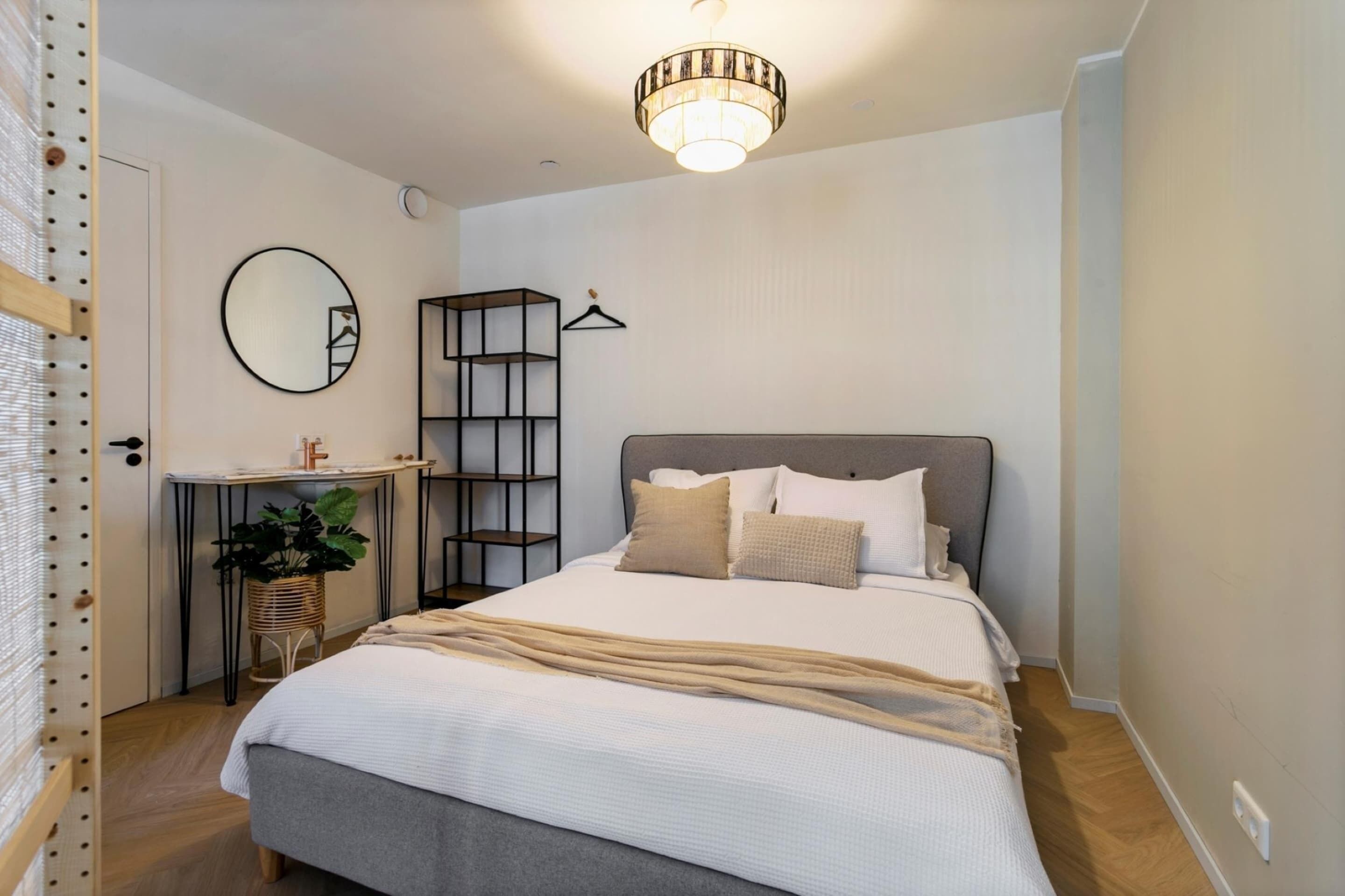 Quarto com cama, mesa de cabeceira, espelho e luminária suspensa.