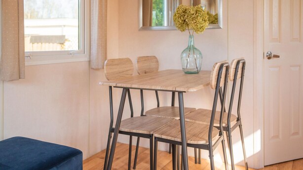 Uma sala de jantar com uma mesa e cadeiras de madeira, um vaso com flores e uma porta.