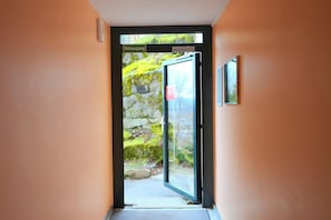 Corredor com porta de vidro que dá para área externa com muro de pedra e vegetação.