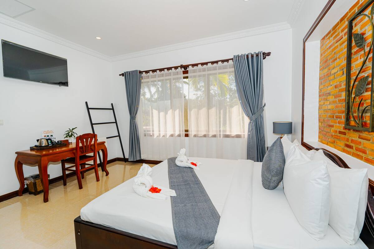 Quarto de hotel com cama, escrivaninha, cadeira e televisão.