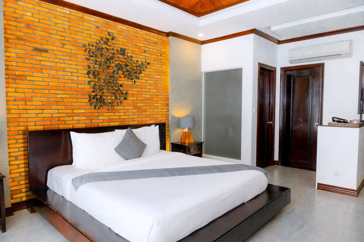 Quarto de hotel com parede de tijolos decorativa, uma cama grande, mesa de cabeceira com abajur e um guarda-roupa.