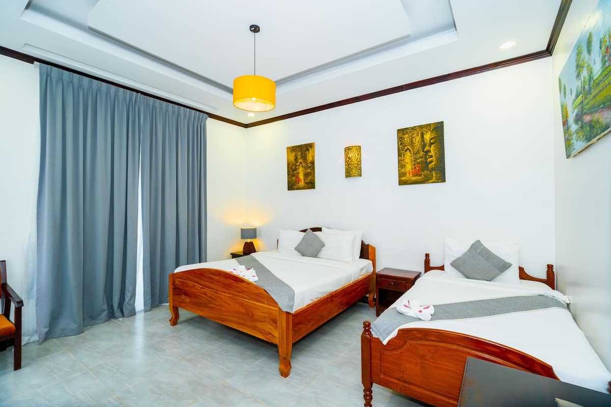 Quarto de hotel com duas camas de madeira, uma janela grande com cortinas, uma luminária no teto e obras de arte nas paredes.