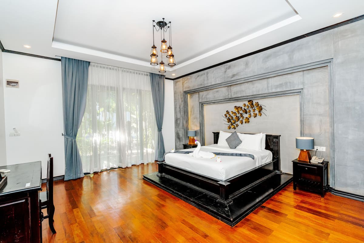 Quarto moderno com uma cama grande, piso de madeira, um candelabro e uma mesa de cabeceira com luminária.