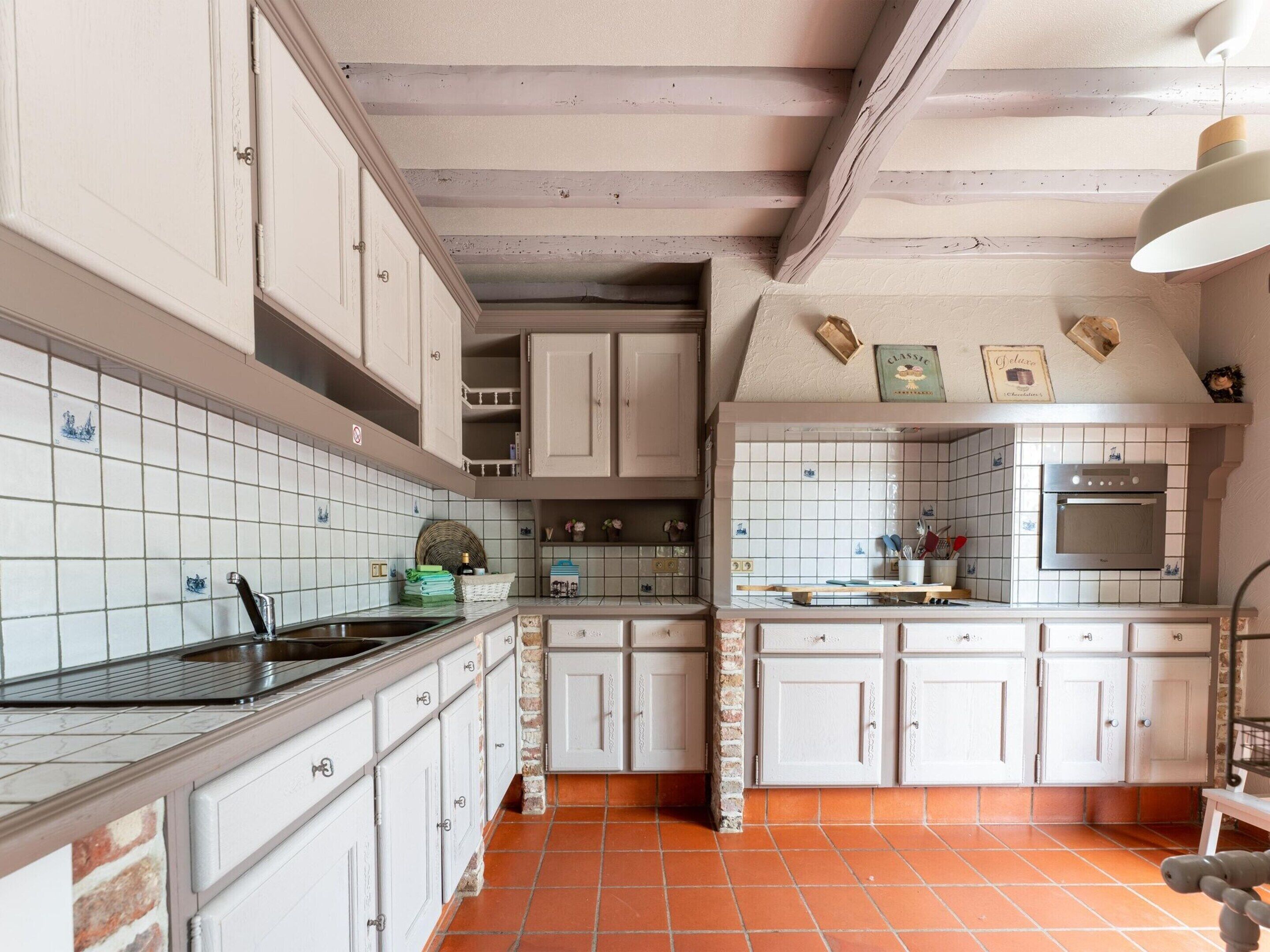 Uma cozinha com armários brancos, painel de azulejos e piso de tijolo.