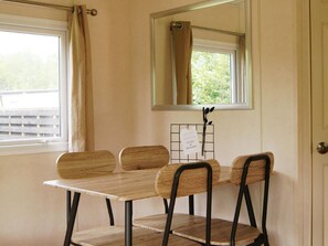 Um quarto com uma mesa de madeira e quatro cadeiras, uma janela com cortina e um espelho na parede.