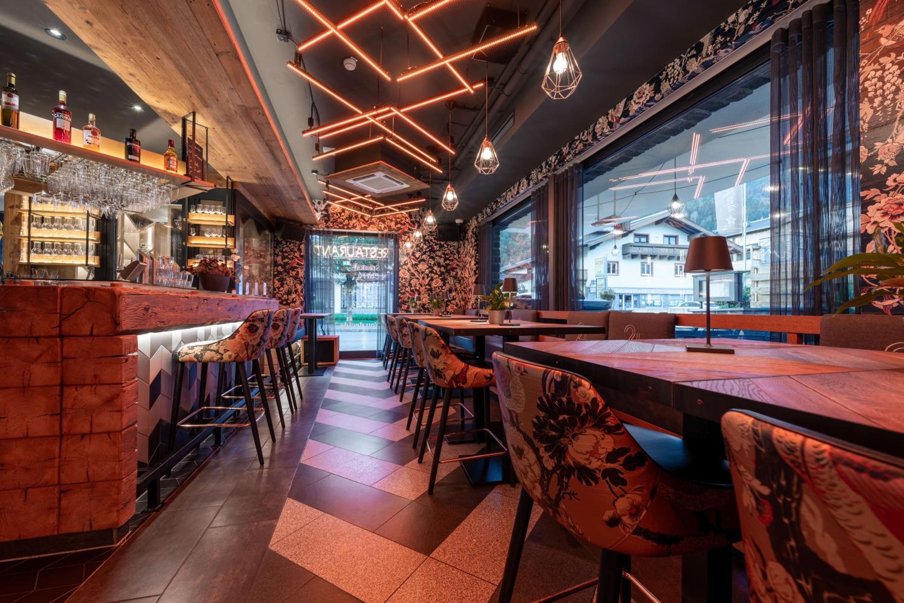 Uma área de bar com piso xadrez, banquetas e balcão com garrafas e copos.
